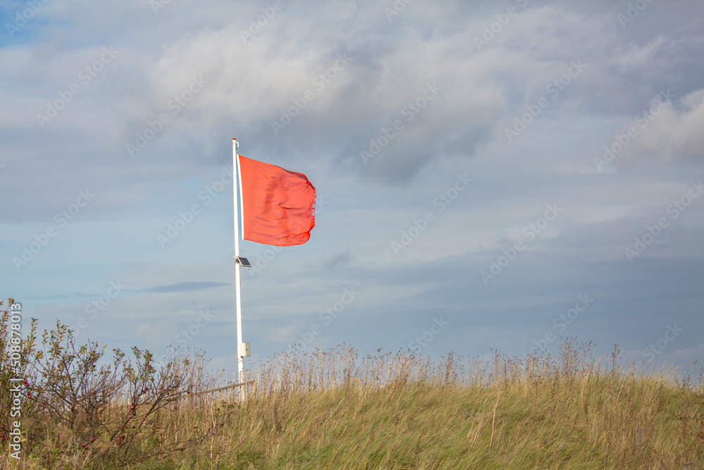 Red flag waving in the wind with small solar panel on the post at ...