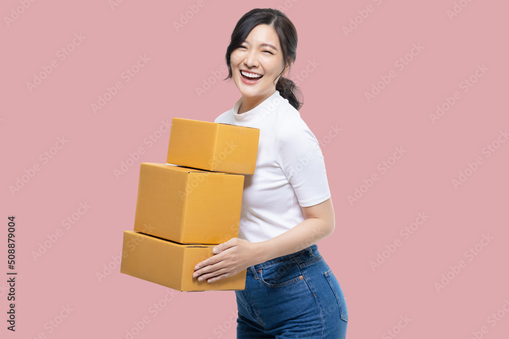 Happy Asian girl holding package parcel boxs isolated on pink screen ...