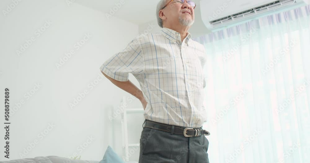 Elderly man Asian has sudden back pain as he gets up from the sofa in ...