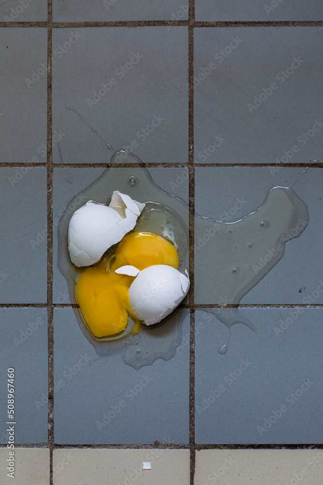 Broken, raw egg on an old tile floor in a kitchen. Accidents will ...