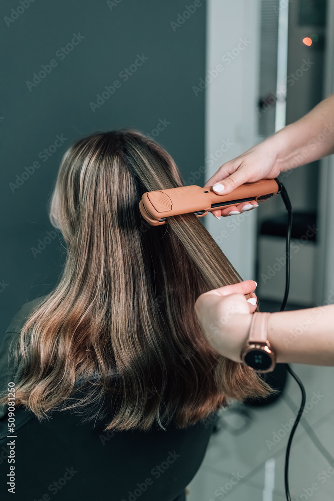 Woman hairdresser straightens brown hair of a beautiful woman using ...