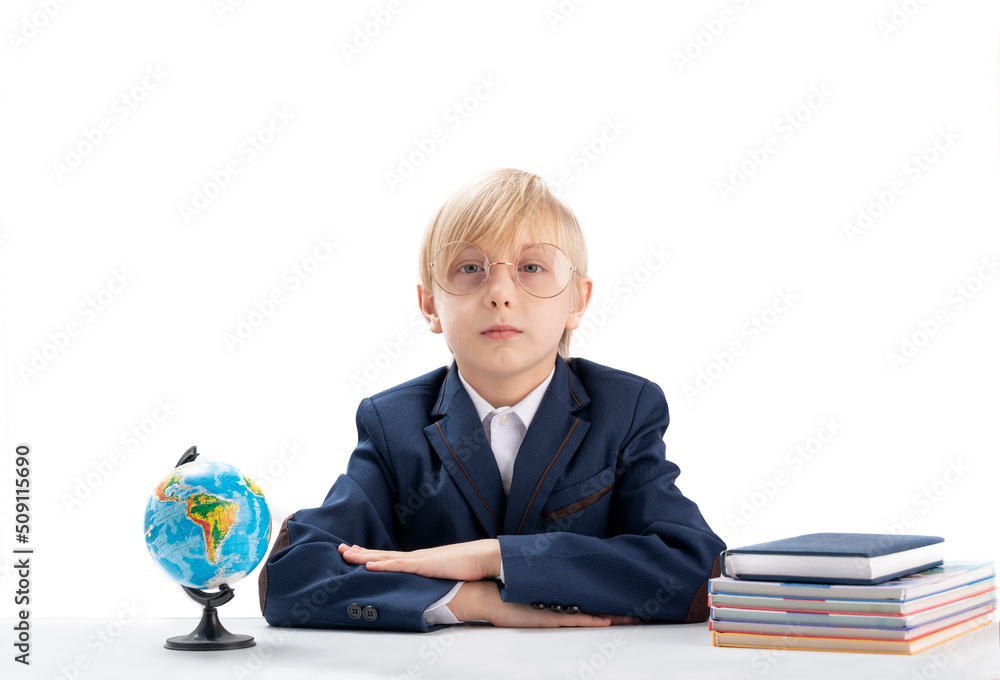Excellent boy sits at table with his hands folded and stares seriously ...