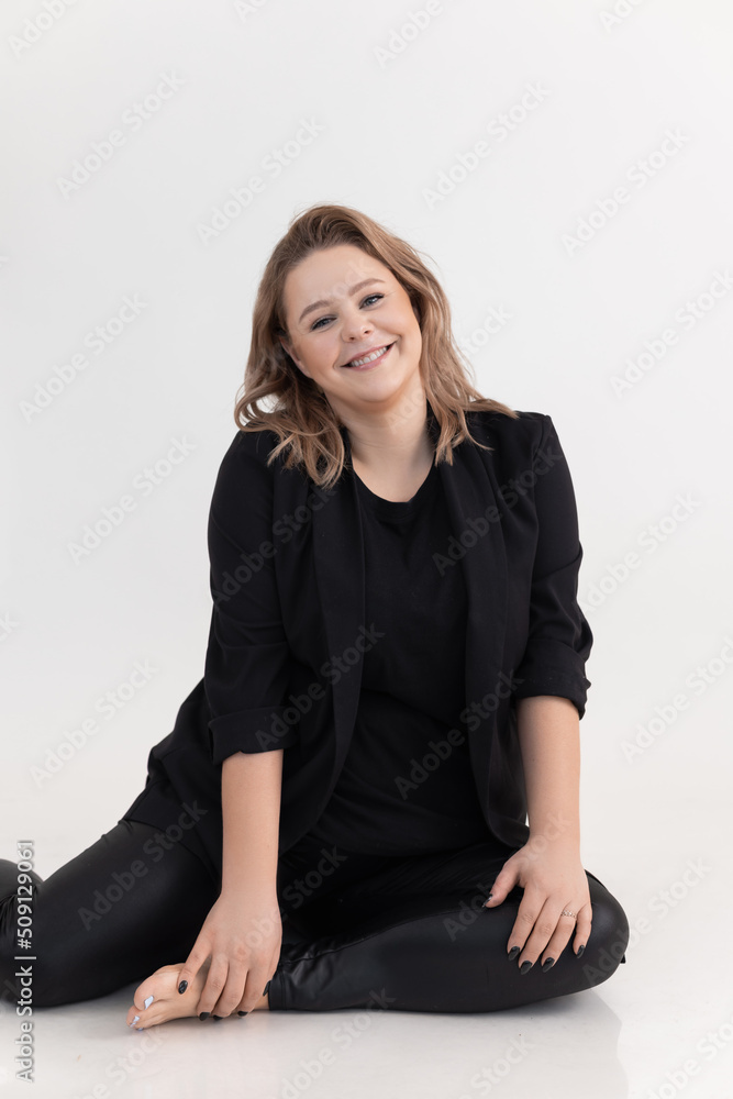 Vertical studio portrait of smiling and plump young woman sitting on ...