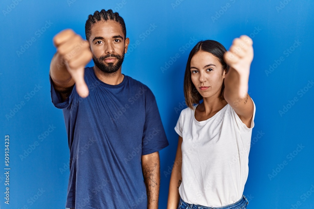 Young hispanic couple standing together looking unhappy and angry ...