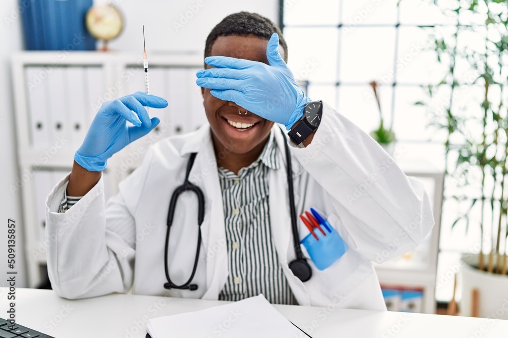 Young african doctor man holding syringe at the hospital smiling and ...