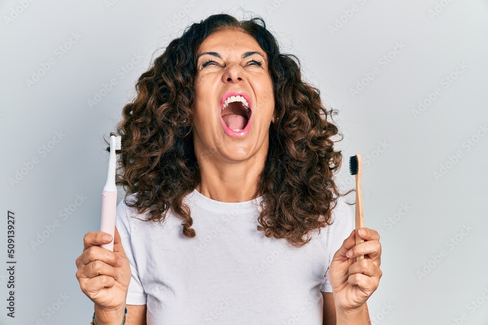 Middle age hispanic woman holding electric toothbrush and teethbrush ...