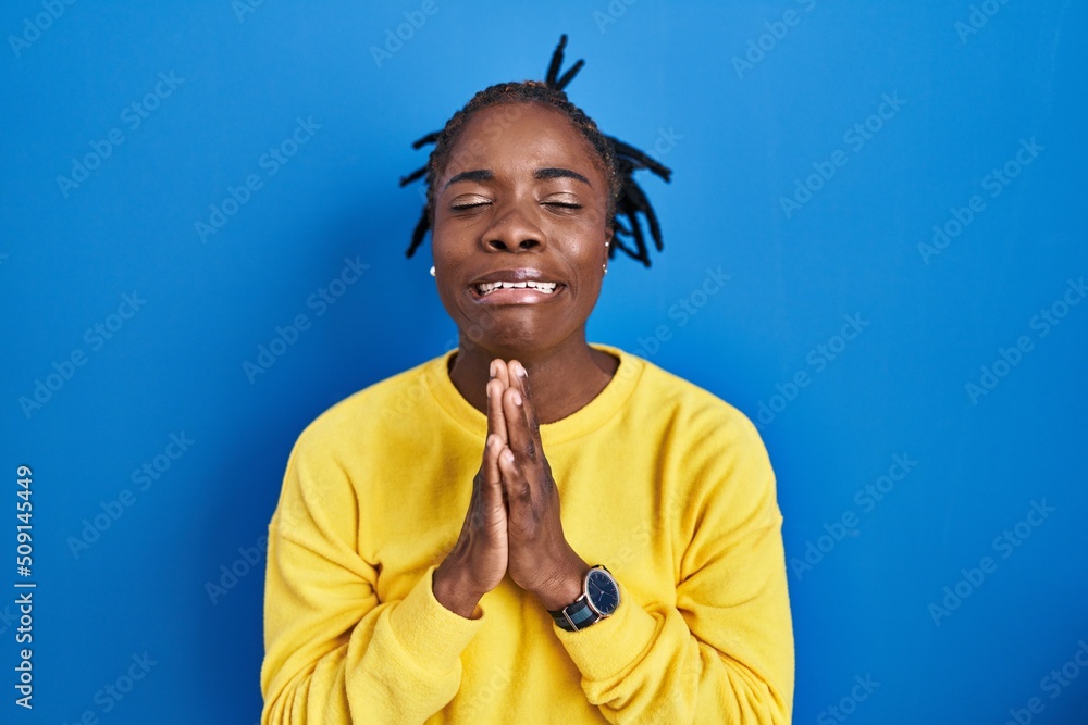 Beautiful black woman standing over blue background begging and praying ...