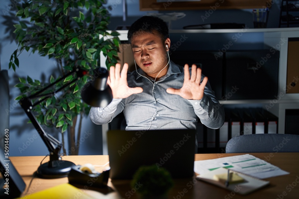 Young chinese man working using computer laptop at night afraid and ...