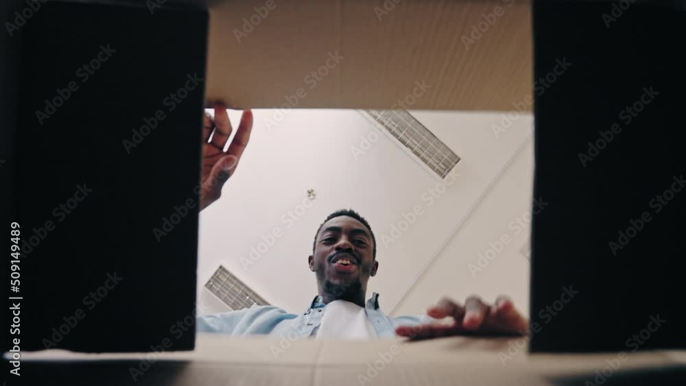 Enthusiastic African American man opening box, surprised by its content ...