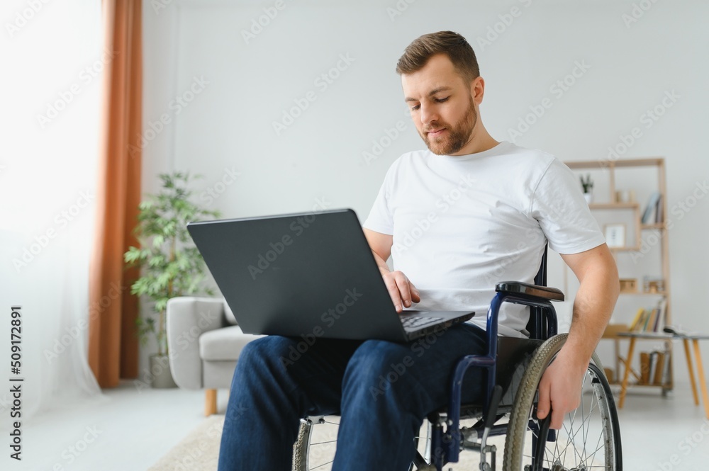 Portrait of smiling disabled male sitting in wheelchair and working on ...