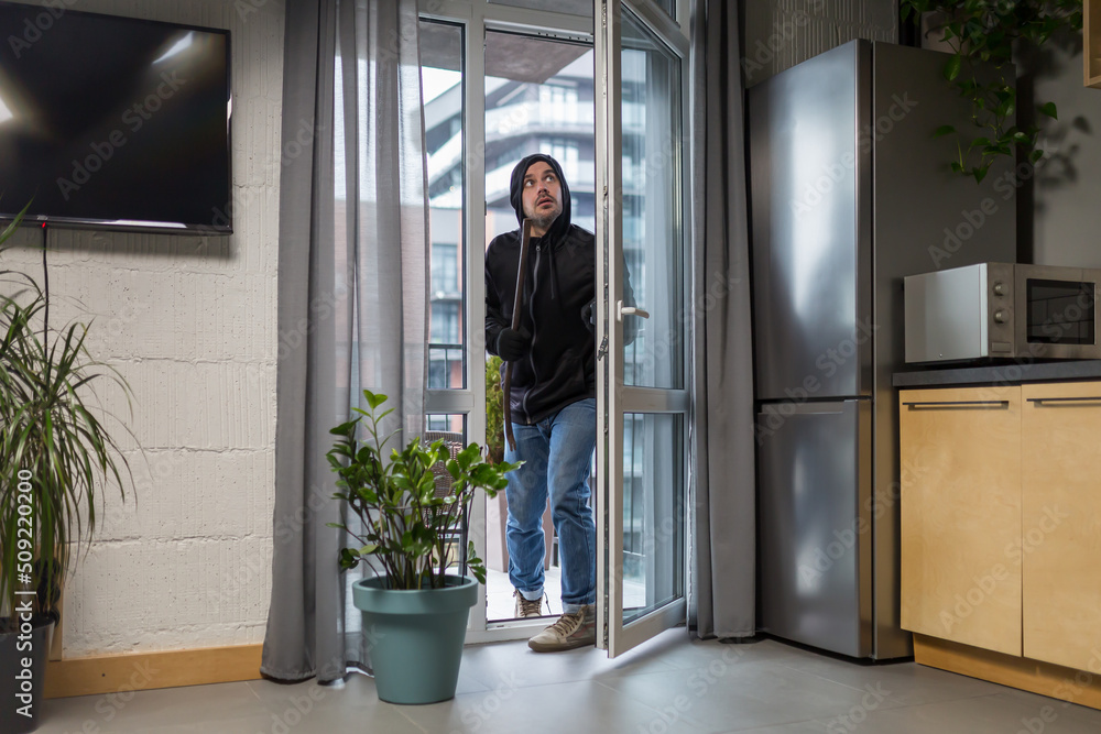 Young male robber in dark clothes carefully and quietly enters through ...
