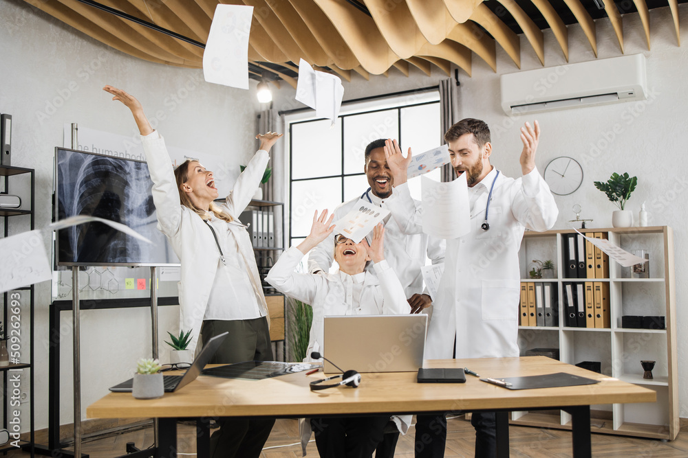 Excited multiracial scientists in white medical uniform laughing and ...
