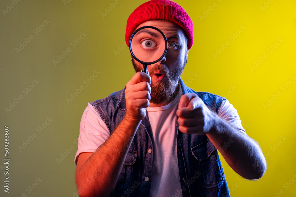 Bearded hipster man standing, holding magnifying glass and looking at ...
