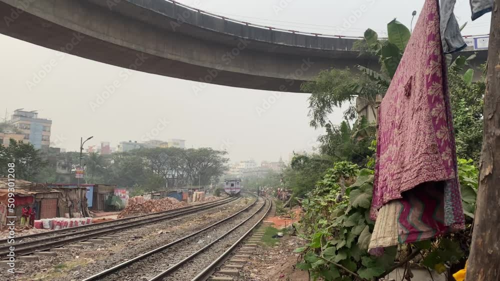 Static shot of a passenger train passing through a poor colony with ...