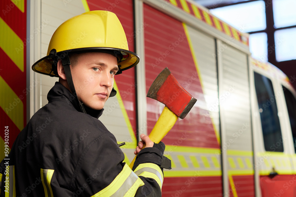 Firefighter fully equipped with helmet and ax in fire truck background ...