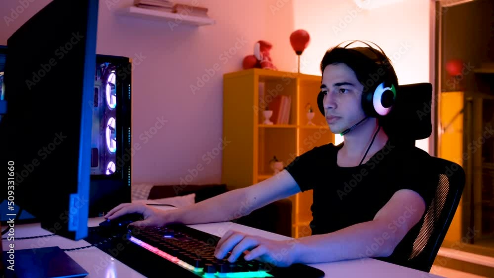 Tired gamer boy is stretching his neck, playing online game in his room ...