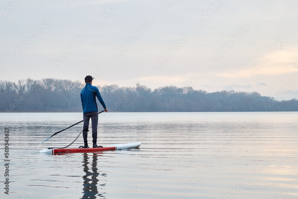 Side view of man on stand up paddle board (SUP) rowing on the river at ...