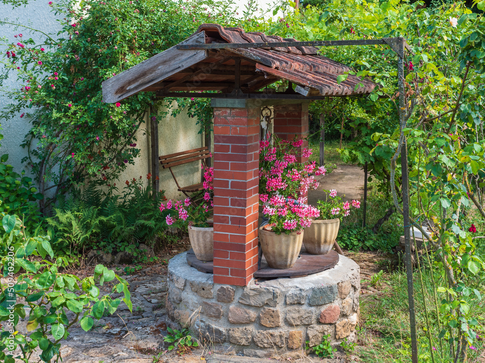 Foto de Vieux puits dans un jardin avec abri en tuile avec des fleurs ...