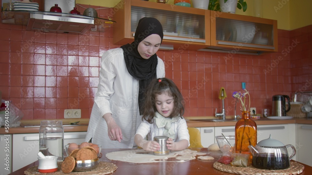 Muslim family spend time in the kitchen. Mom and daughter cut out dough ...