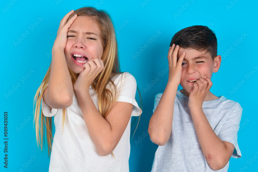Young gloomy two kids boy and girl standing over blue studio background ...