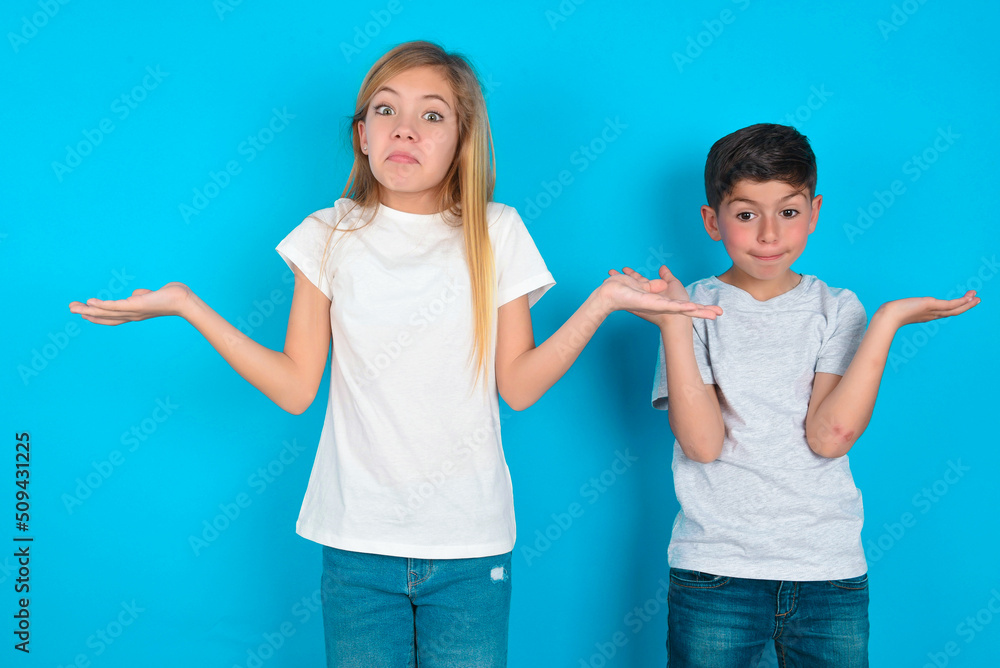 Puzzled and clueless two kids boy and girl standing over blue studio ...