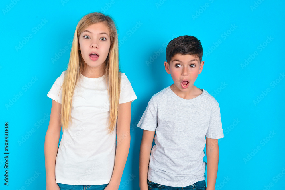 two kids boy and girl standing over blue studio background having ...