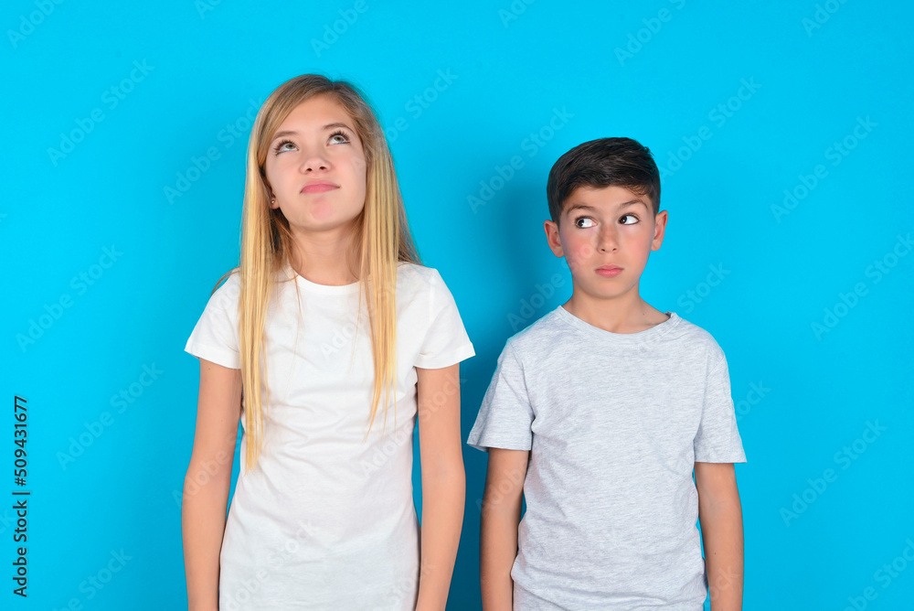 two kids boy and girl standing over blue studio background has worried ...
