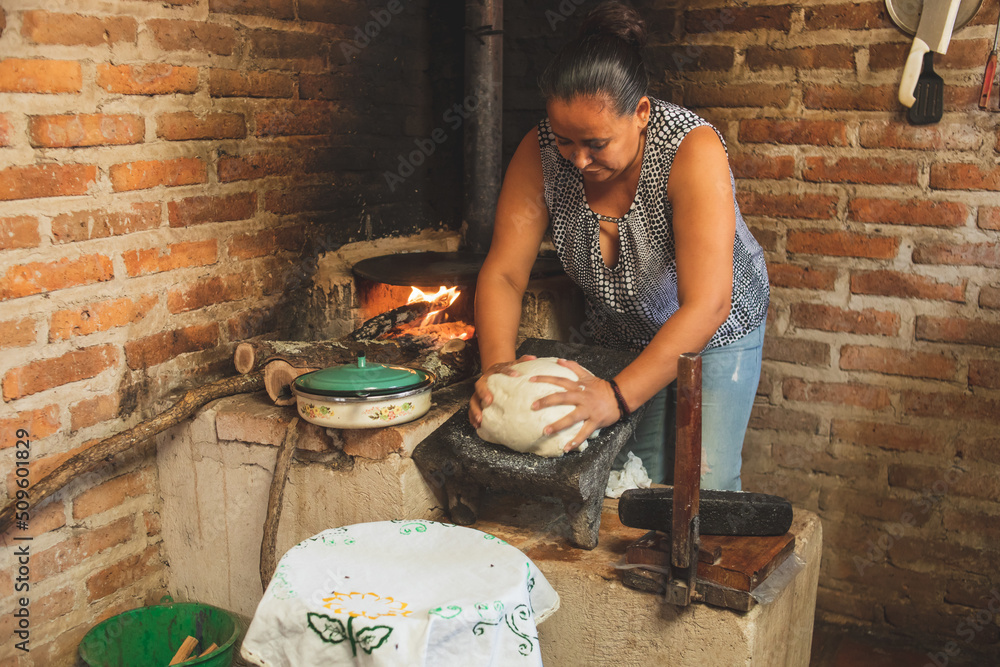 Mujer mexicana torteando maza de maíz en un metate y una estufa de leña ...