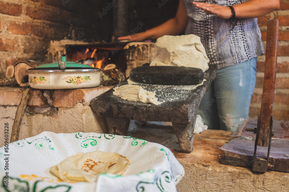 Mujer mexicana torteando maza de maíz en un metate y una estufa de leña ...