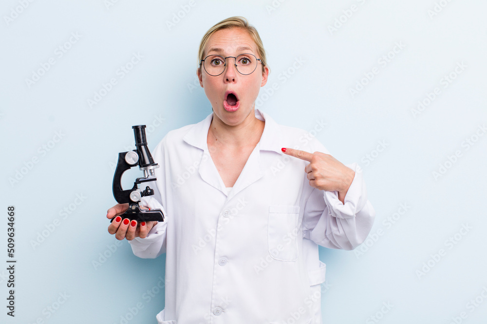 young adult blonde woman looking shocked and surprised with mouth wide ...