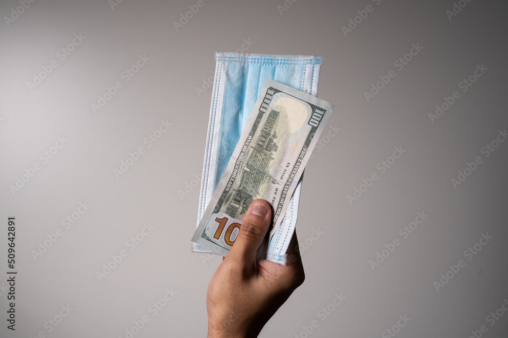 Hand holding the surgical mask and 100 US dollar bill with isolated ...