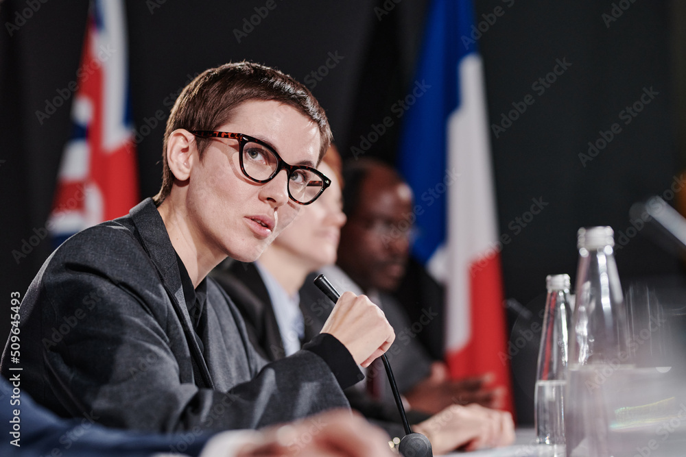 Female speaker in eyeglasses holding microphone and presenting her ...