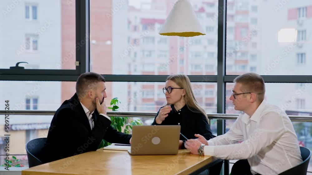 Little meeting of colleagues in the office. People sit at desk, talk ...