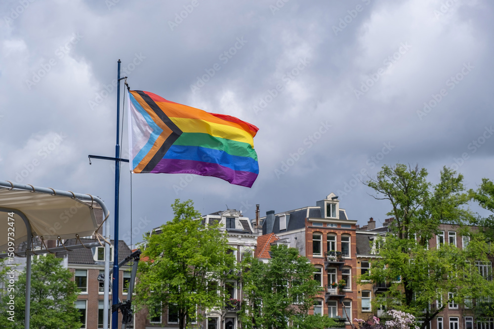 Gay Pride, New Progress LGBTQ rainbow flag waving on a pole, cloudy sky ...
