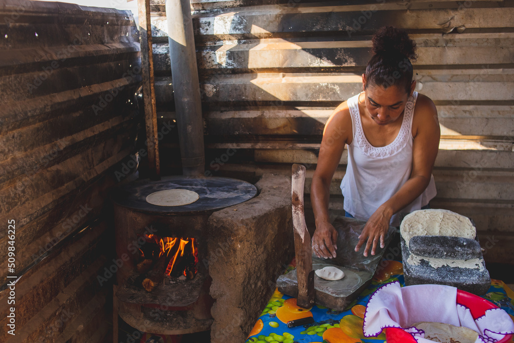 Fotka „Mujer mexicana torteando maza de maíz en un metate y una estufa ...
