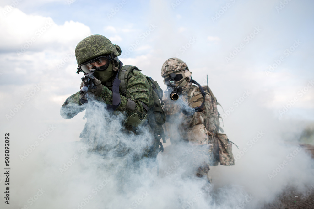Military soldiers in the smoke storm the enemy by firing their weapons ...