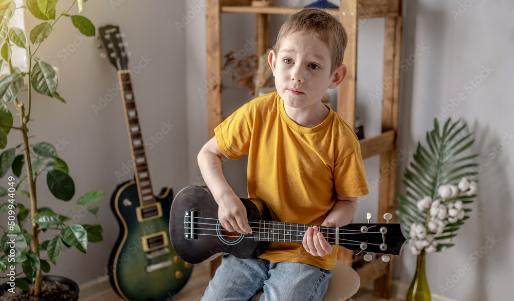 Cute cheerful boy is playing the ukulele in the music room. Joyful ...