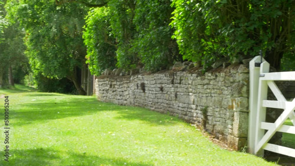Pan shot of a traditional white painted wooden gate and an old stone ...