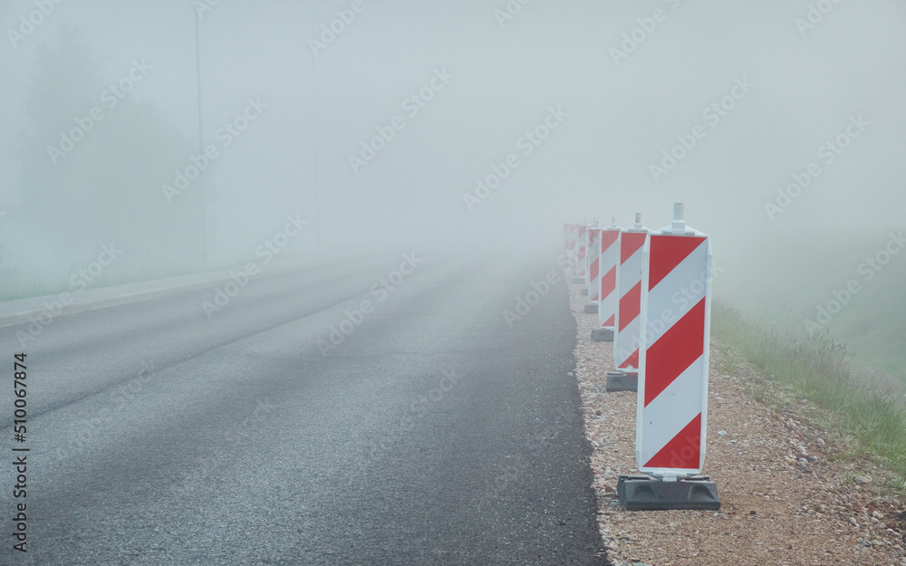 An empty new asphalt road (hghway) in a thick fog. Red and white ...