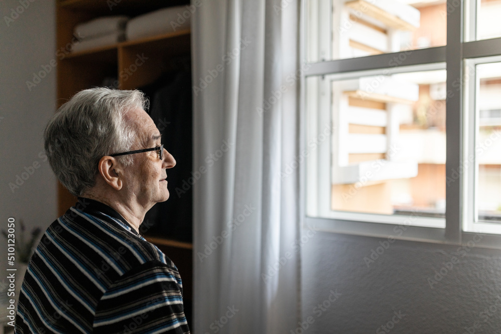 Elderly man looking out the window of his room Stock Photo | Adobe Stock