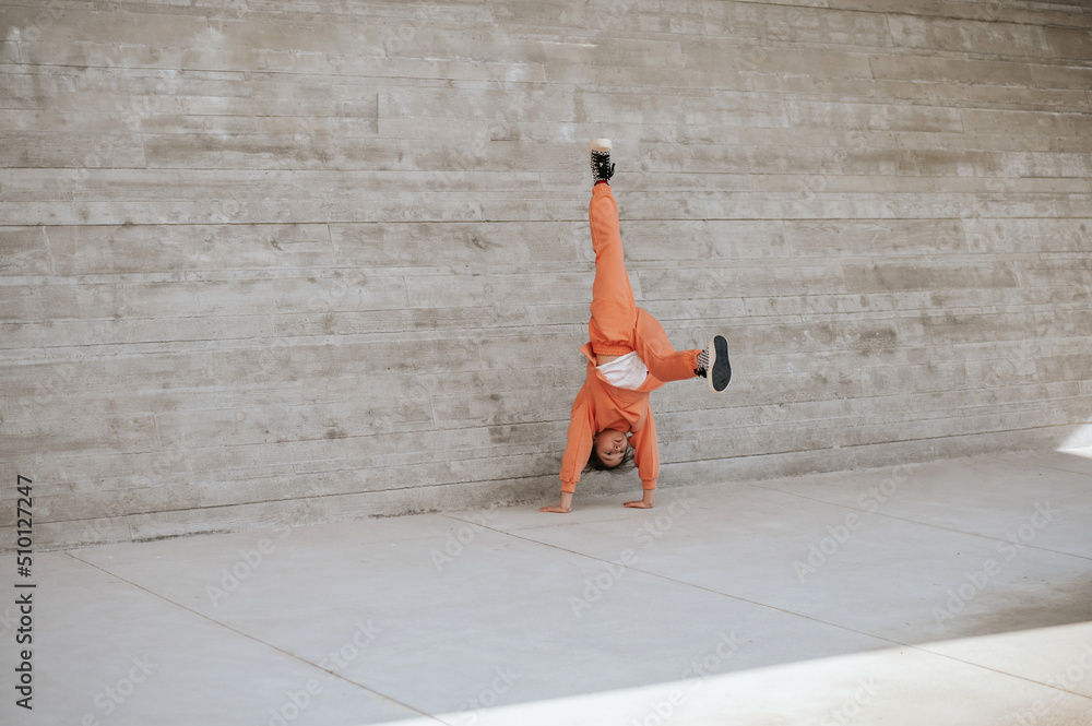 Young girl in workout clothes does handstand against concrete wall ...