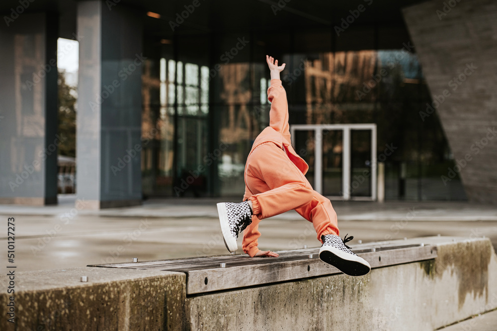Young girl in runners jumps over concrete bench. Stock Photo | Adobe Stock