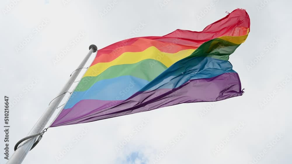 LGBTIQ flag waving on the wind on flagpole in town. A symbol of the ...