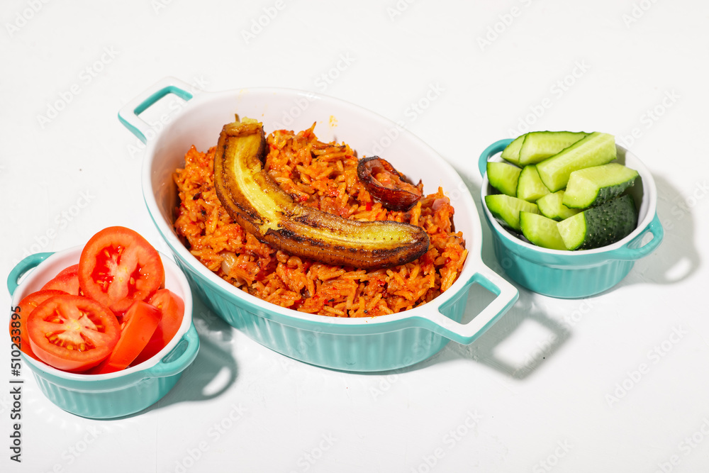 Jollof rice with fried banana. Fresh vegetables - tomato and cucumber ...