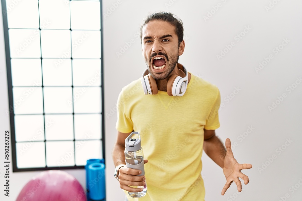 Young hispanic man wearing sportswear and drinking water at the gym ...