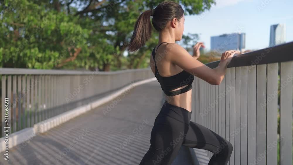 Asian fit girl doing post work out stretching by holding on to fences ...