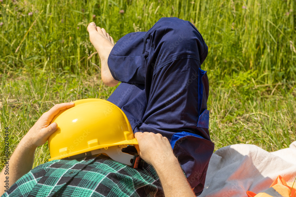 Worker relaxes lying on a meadow with a helmet and in working clothes ...