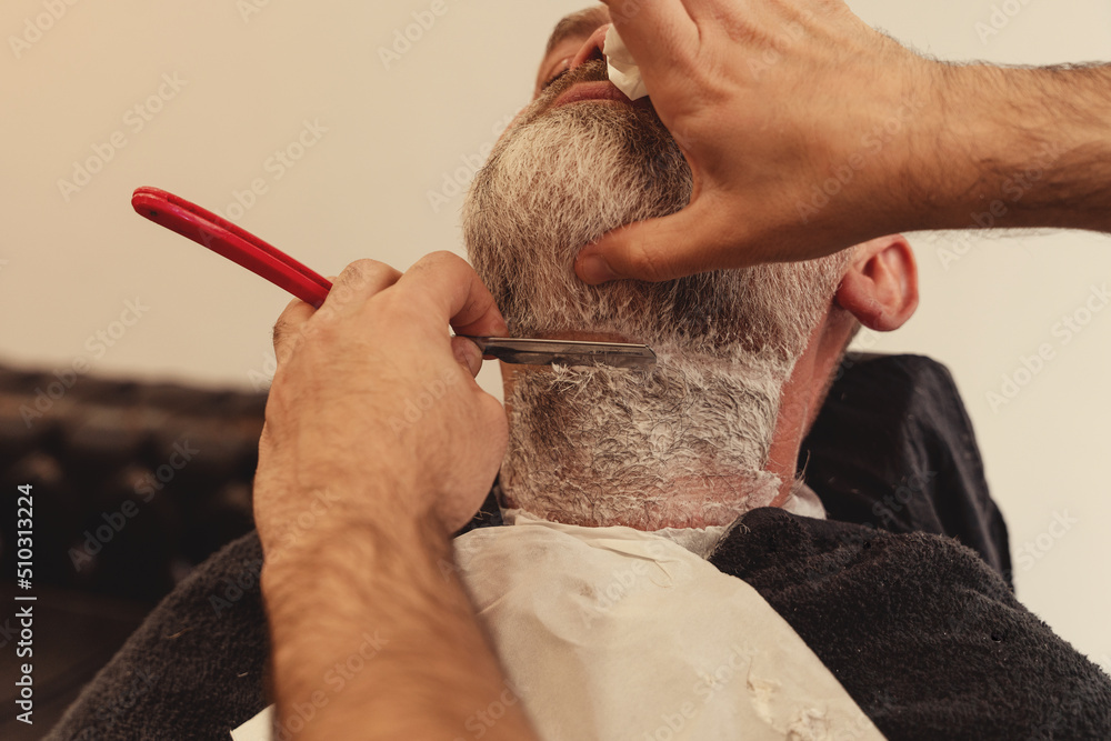 Shaving with a straight razor in a barbershop. A bearded old man being ...