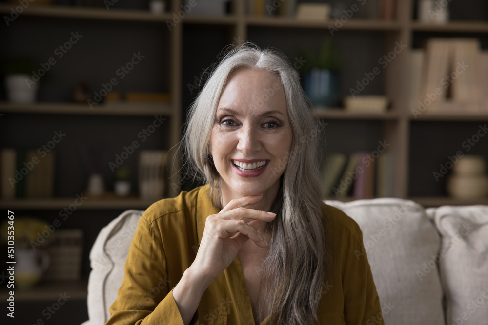 Beautiful older 50s woman sit on sofa put chin on hand staring at ...
