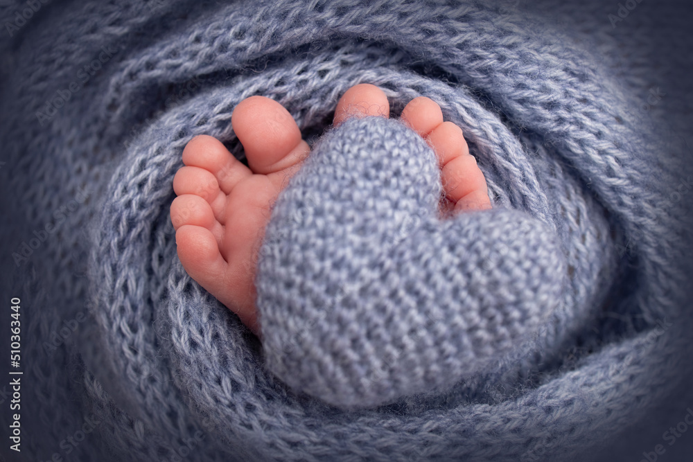 Knitted dark blue heart in the legs of a baby. Soft feet of a new born ...